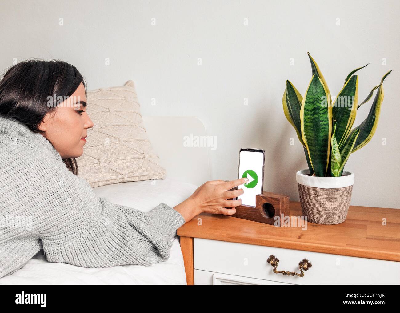 A young beautiful female on a bed of a cozy room going to press the ...