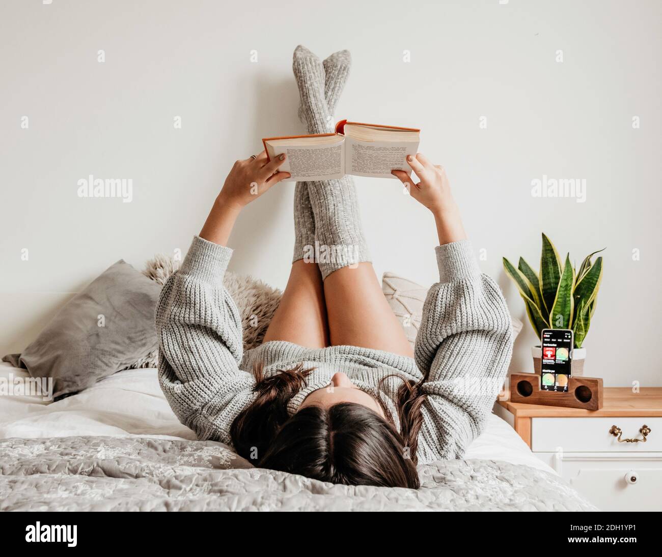 A young female reading a book on the bed with the legs up on a wall in ...