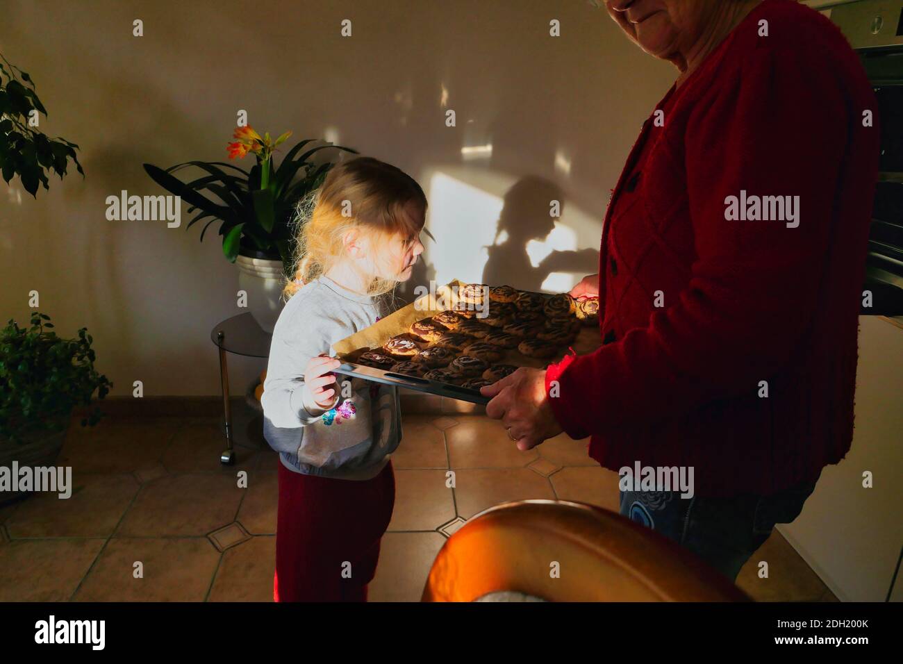 Little girl smelling freshly baked cinnamon rolls in tray. Grandmother ...