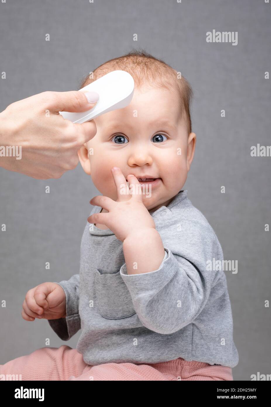 Pediatrician or nurse checks baby girl's body temperature using infrared forehead thermometer ...