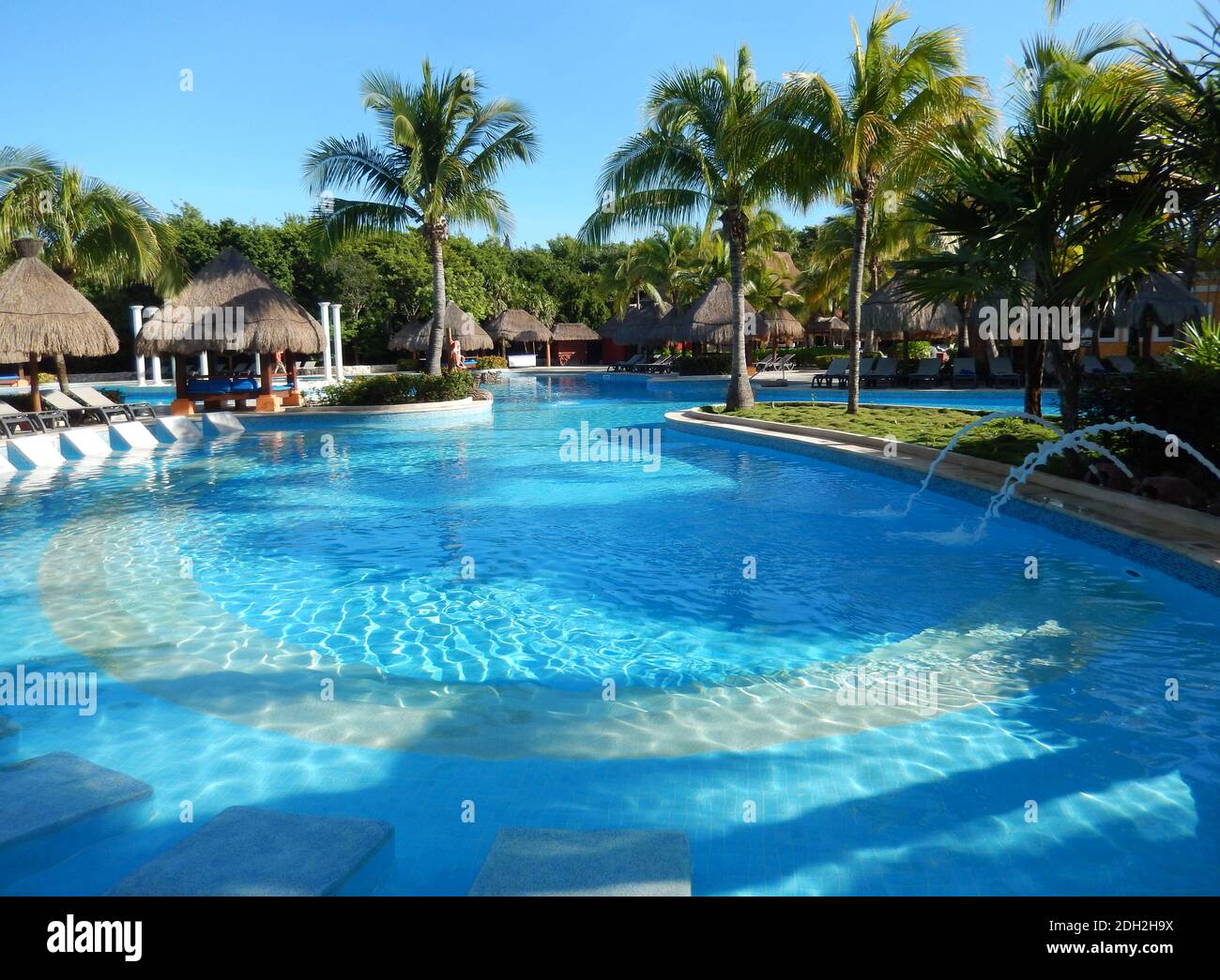 Pool sitting area with straw umbrellas, chaise longue chairs and palm ...