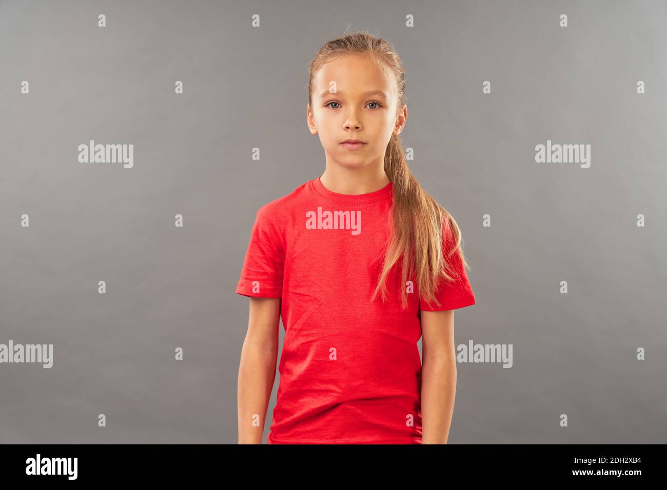 Waist up of cute girl in red shirt looking at camera with serious ...