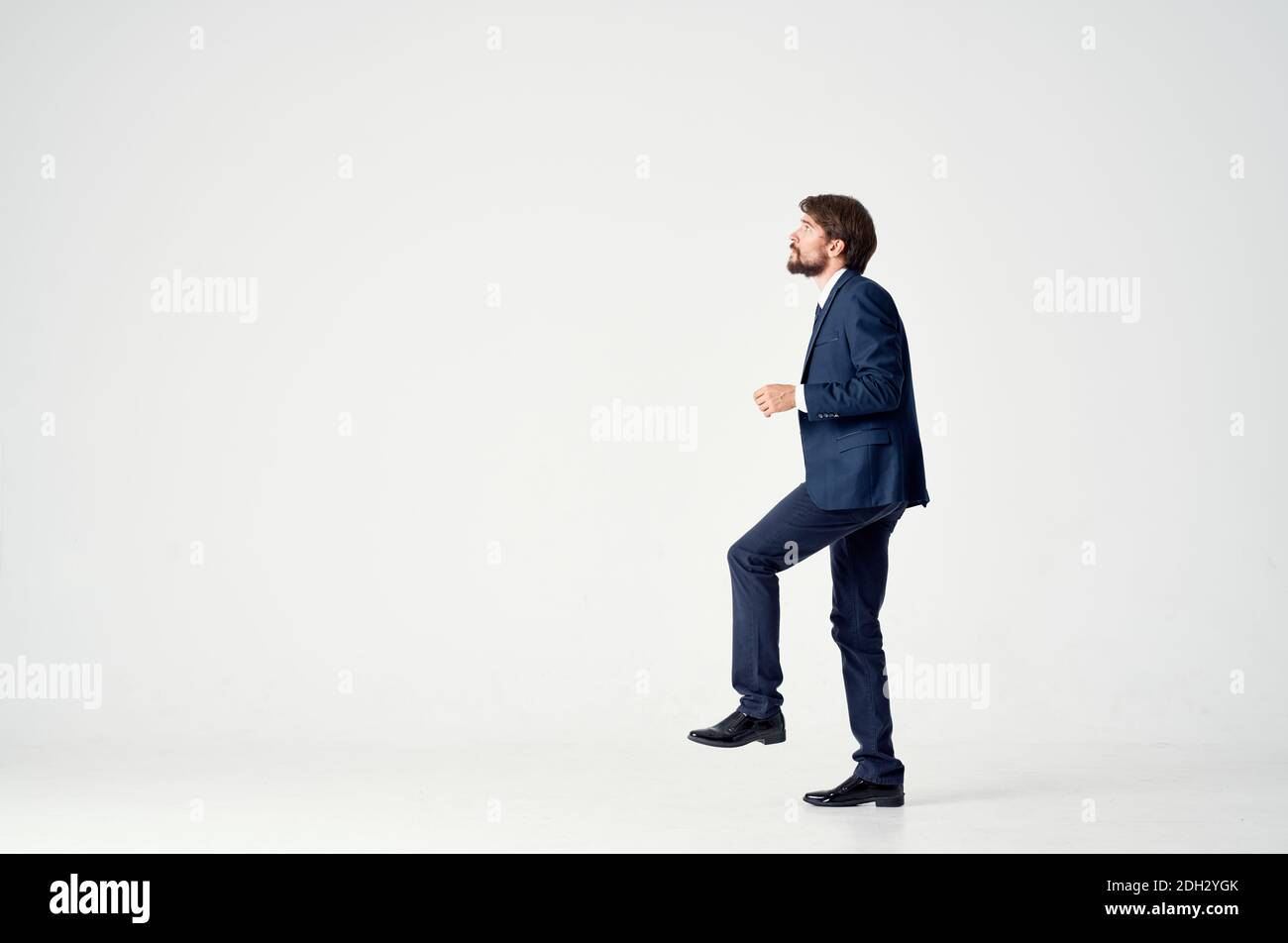 business man in a blue suit stands on one leg on a light background ...