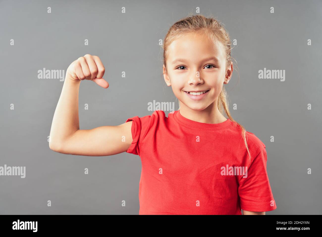 Cute female child showing her arm muscles and smiling while standing ...