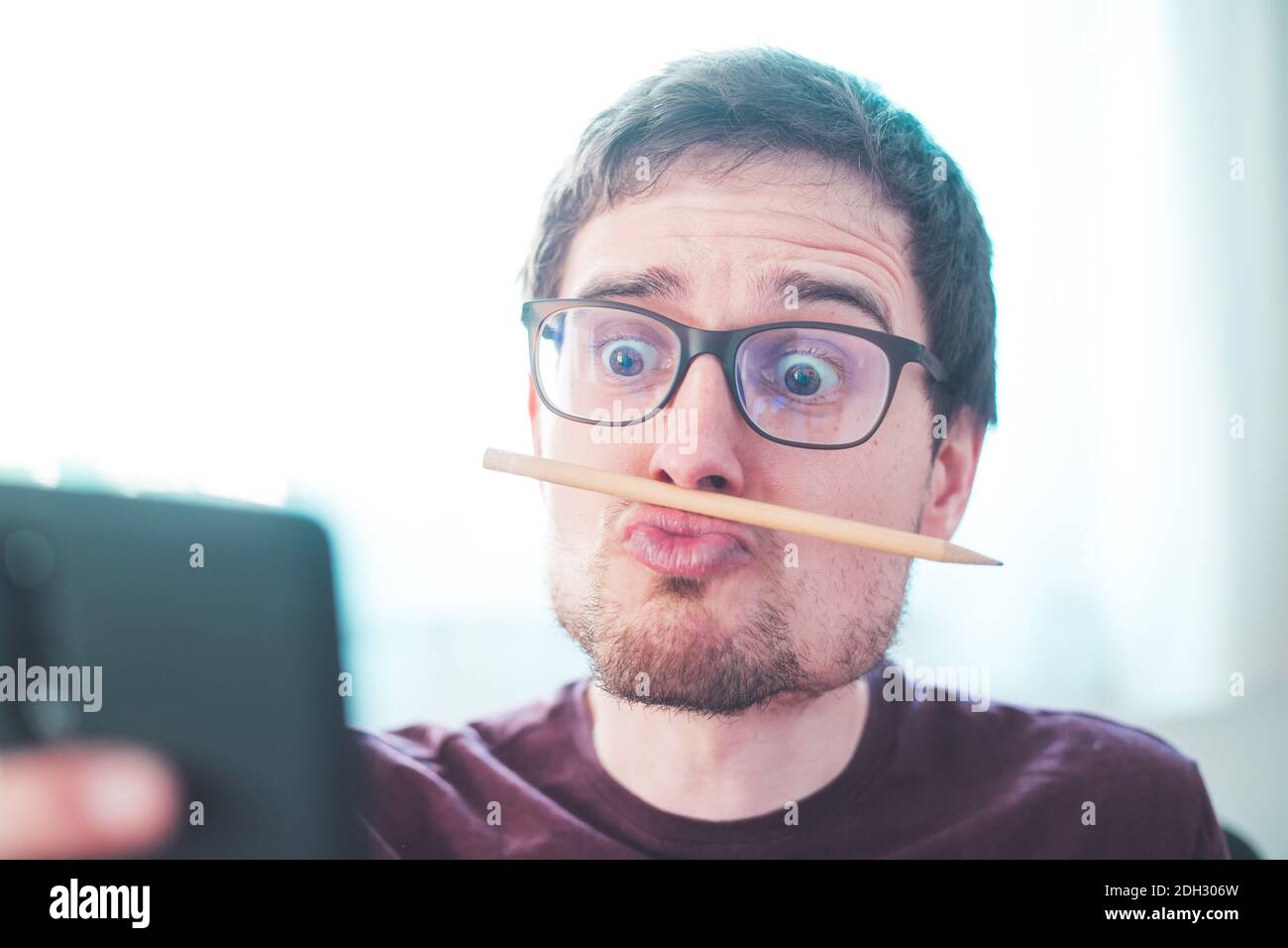 Fooling around at home. Bored young man with a trapped pencil between ...