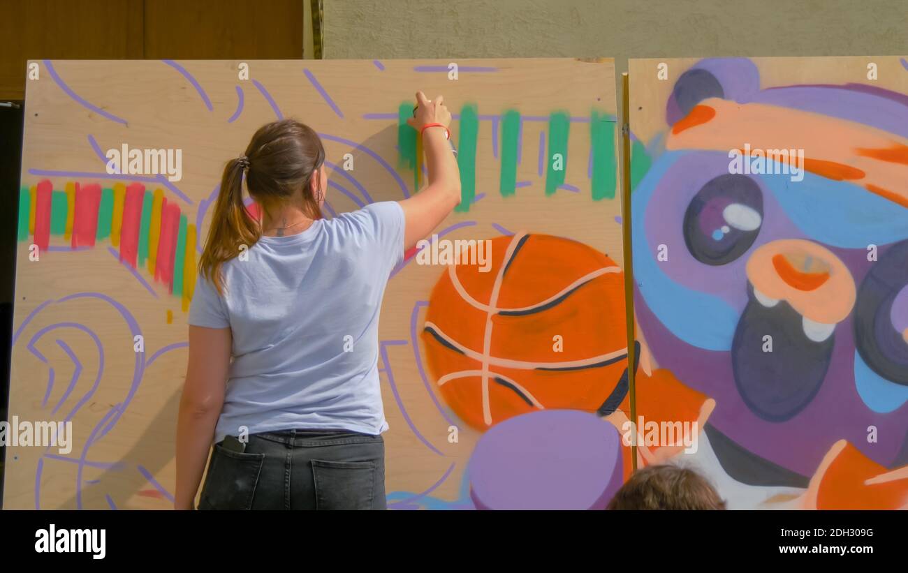 Young woman spraying paint from spray can on wooden surface - back view ...