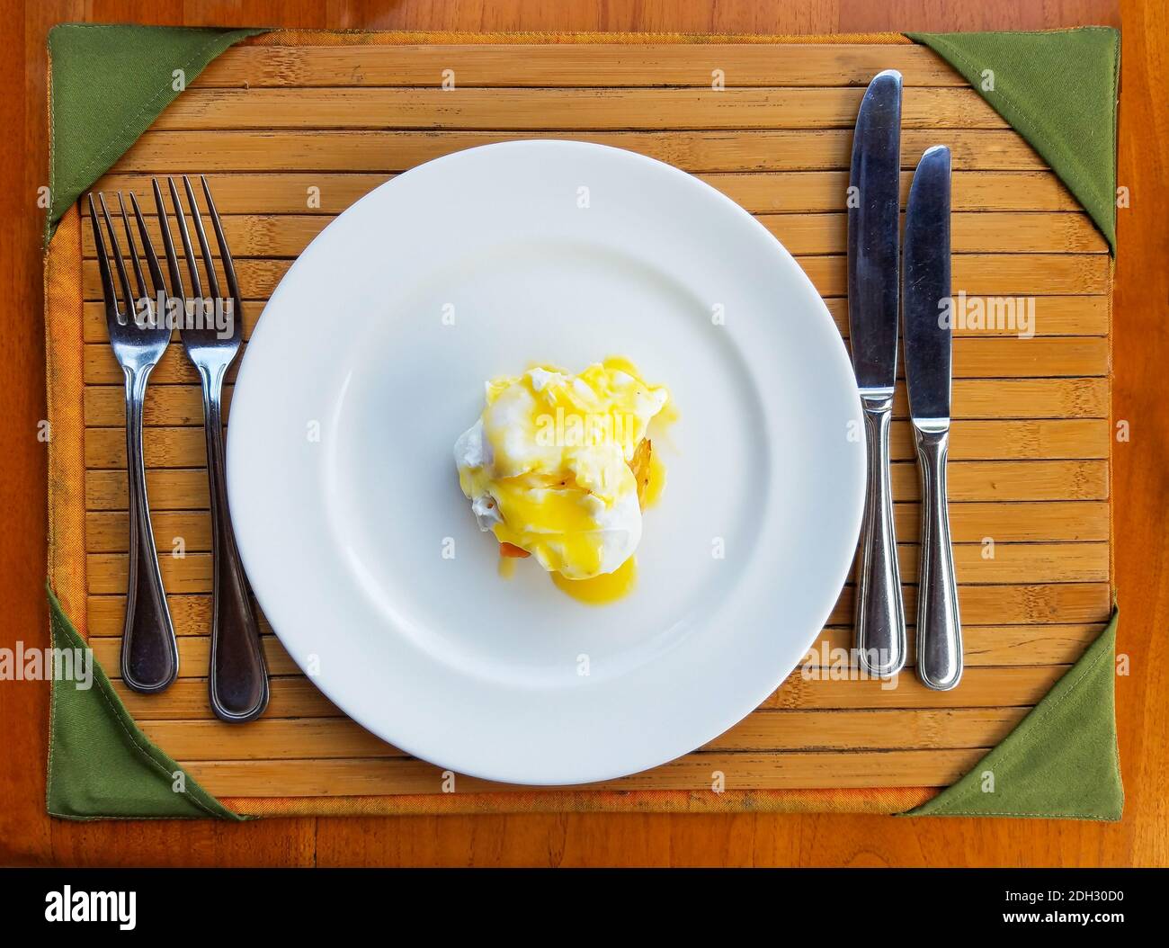 Breakfast setting with a plated egg Benedict and silverware on a bamboo ...