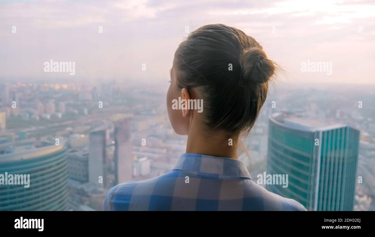 Back view of woman looking at cityscape through window of skyscraper ...