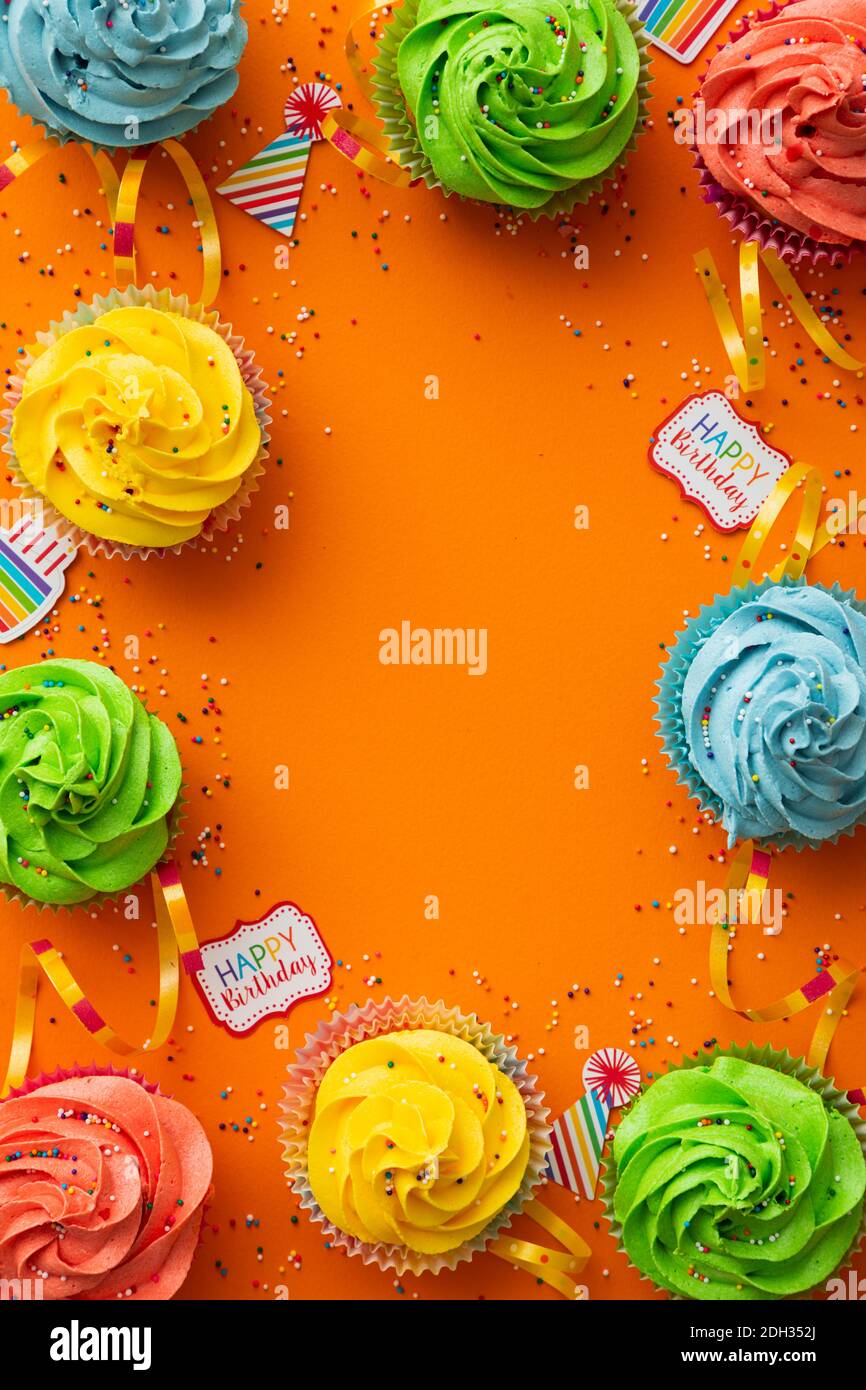 Colorful birthday cupcakes arranged on an orange background with ...