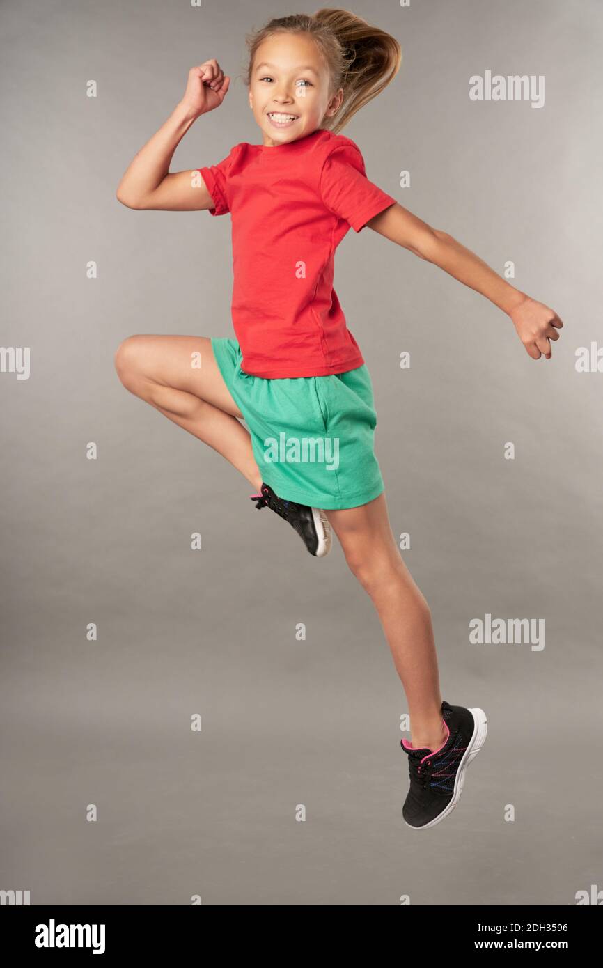 Adorable girl in shorts looking at camera and smiling while jumping in ...