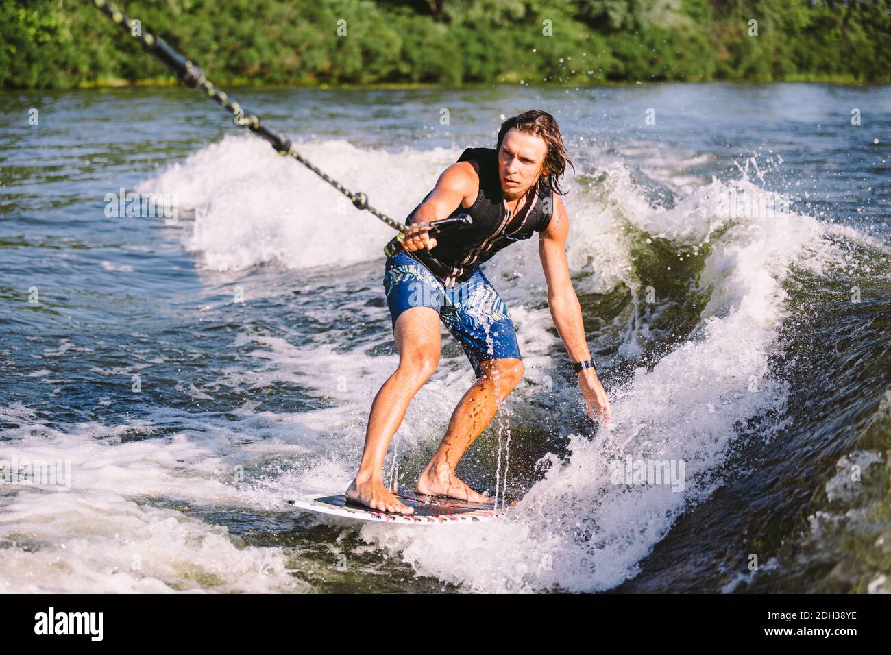 Active wakesurfer jumping on wake board down the river waves. Surfer on ...