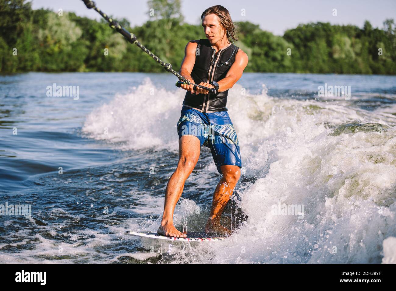 Beautiful long haired blond wakesurf in vest on board along waves of ...