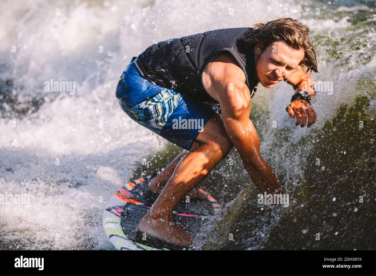 Young athletic man with long hair wakesurfing on waves of river in ...