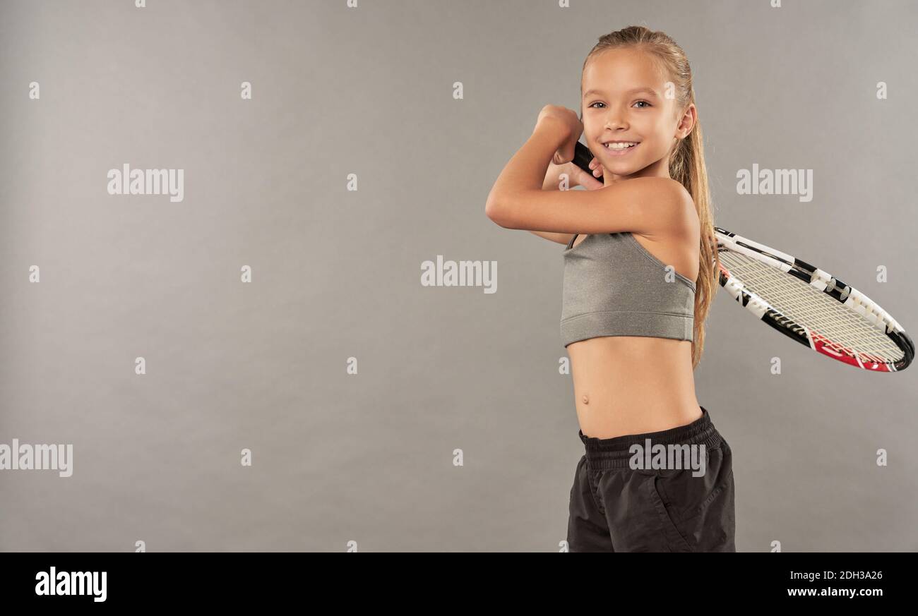 Adorable girl in crop top holding tennis racket and smiling while ...
