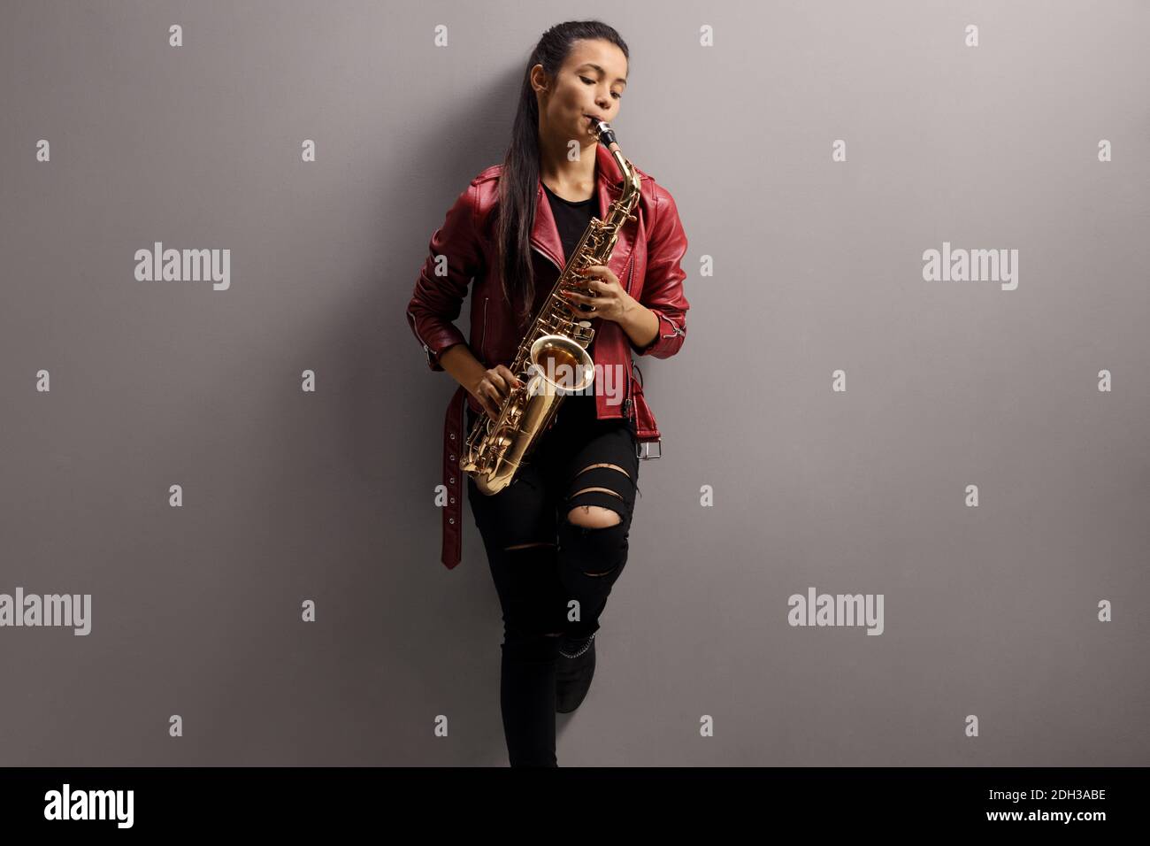 Beautiful woman leaning on a gray wall and playing sax Stock Photo - Alamy