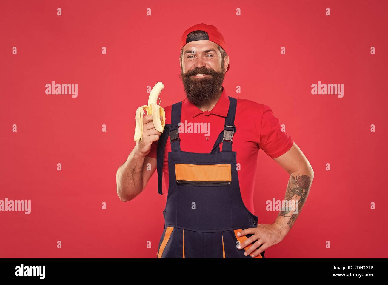 Have healthy snack. Bearded man in uniform and cap eating banana ...