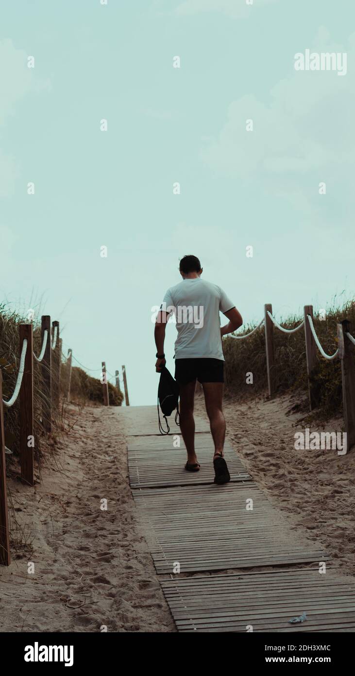A back view of a walking man holding a backpack on the beach in Miami ...