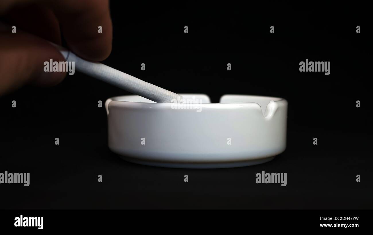 A man holds a cigarette in his hand,flicking ashes into an ashtray ...