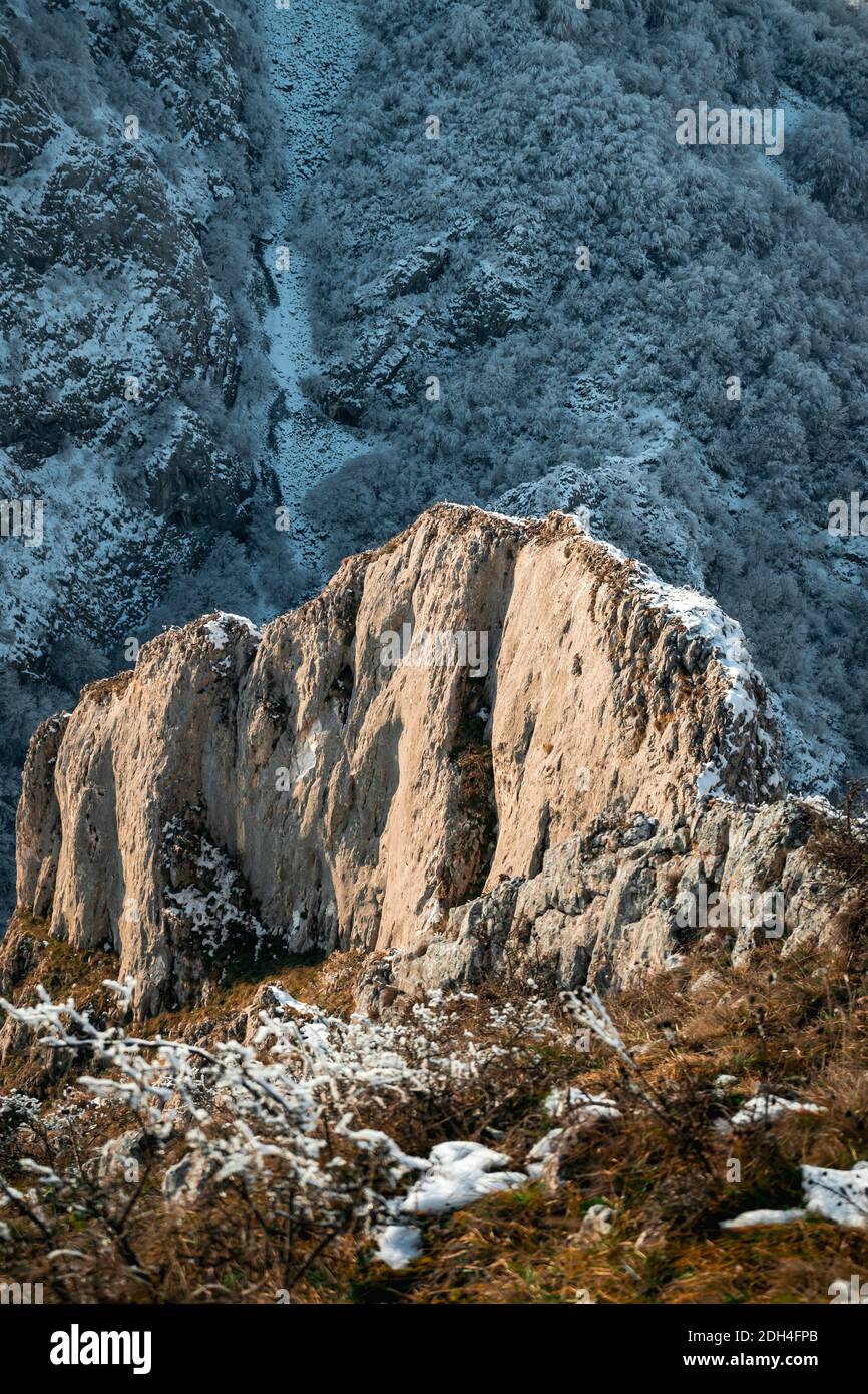 A vertical shot of a cliff covered in snow in front of a higher rock ...
