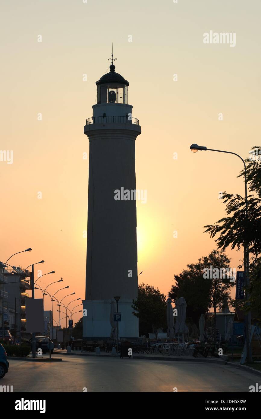 the sun rising behind the lighthouse on the promenade of the city ...