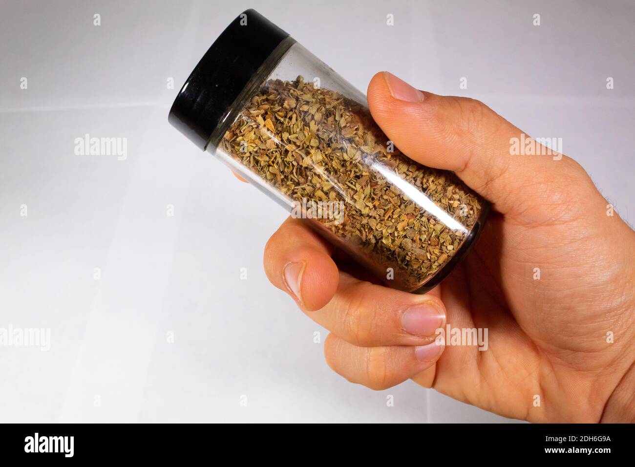 A man's hand holding a bottle of spices for cooking on a white ...