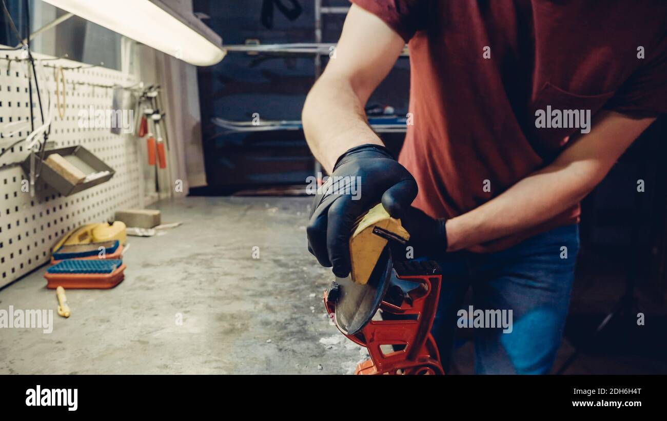 Male worker of ski service workshop doing sharpening and repair of skis ...