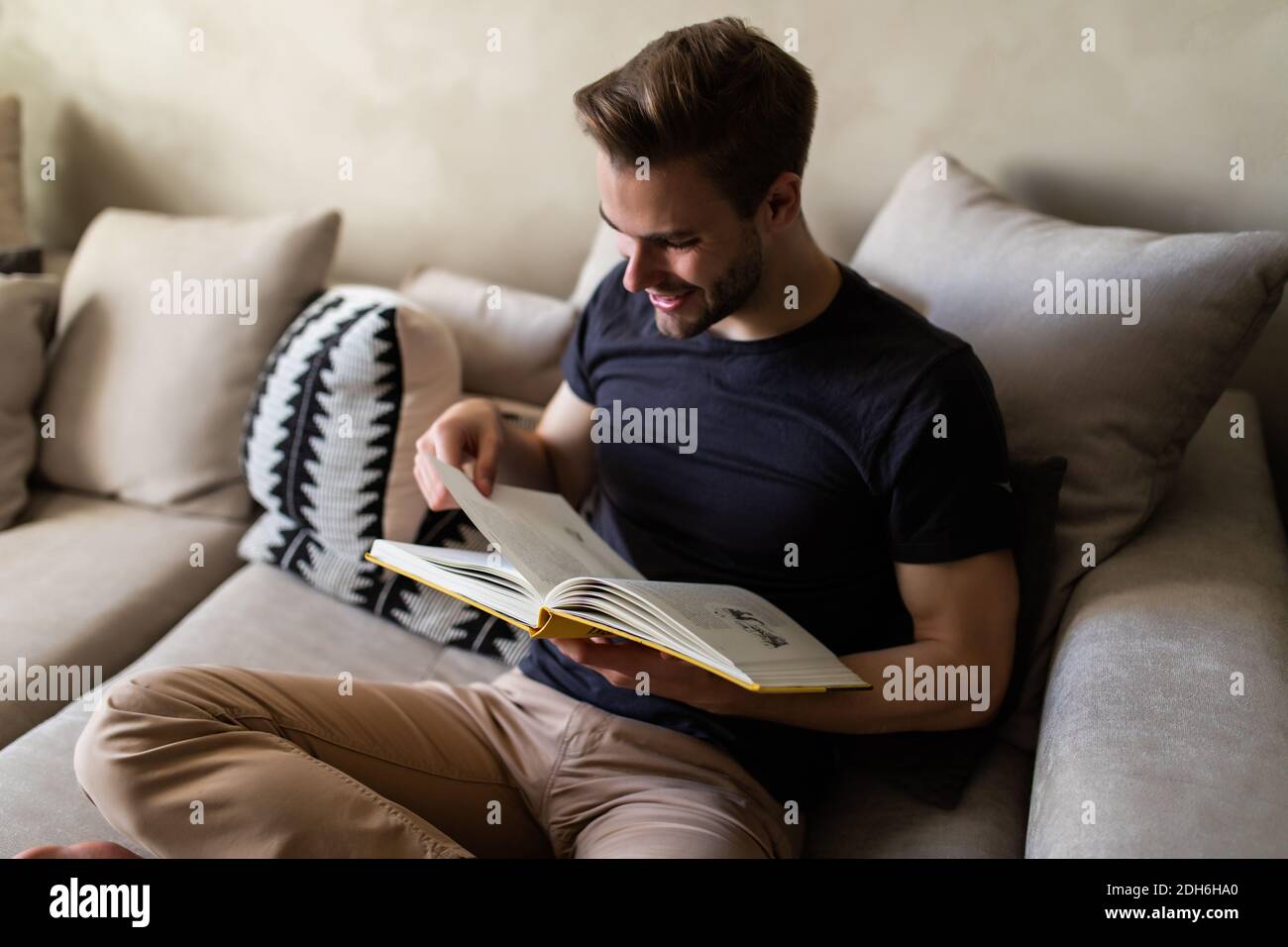 Smiling relaxed man reading a book lying on sofa Stock Photo - Alamy