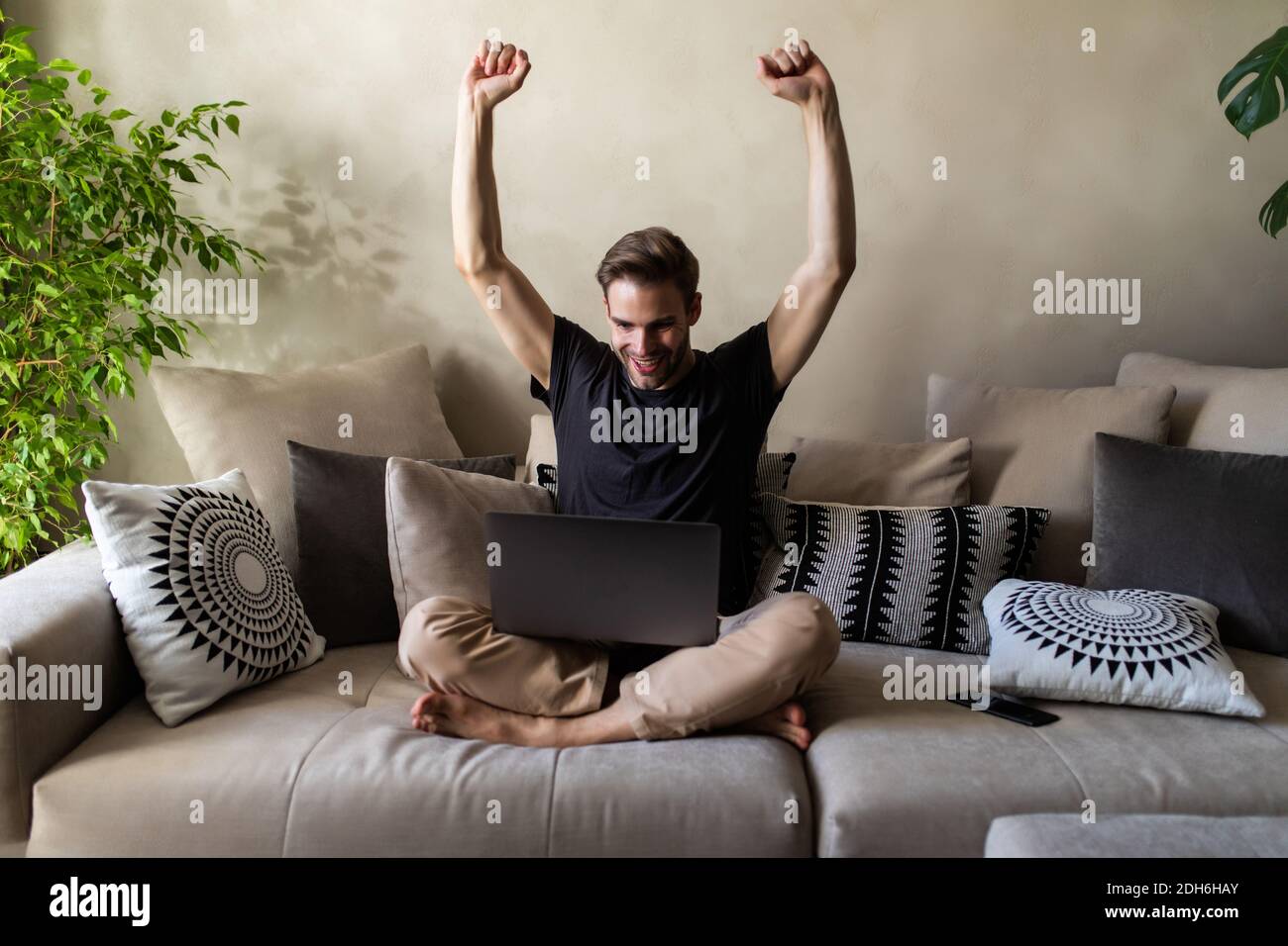 happy excited young man with laptop at home sitting on a couch Stock ...