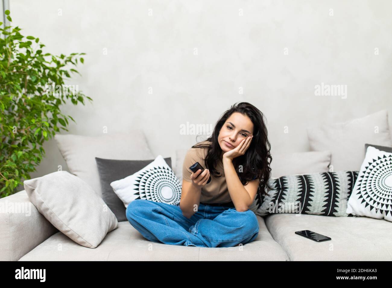 Young woman changing TV channels with remote control sitting on sofa at ... Young woman changing TV channels with remote control sitting on sofa at ...