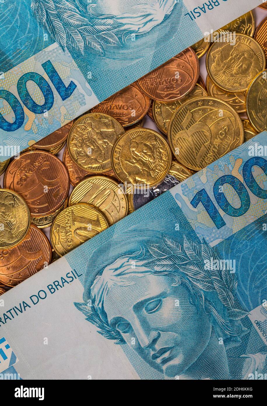 A vertical top view of two Brazilian 100 Reais banknotes with coins in ...