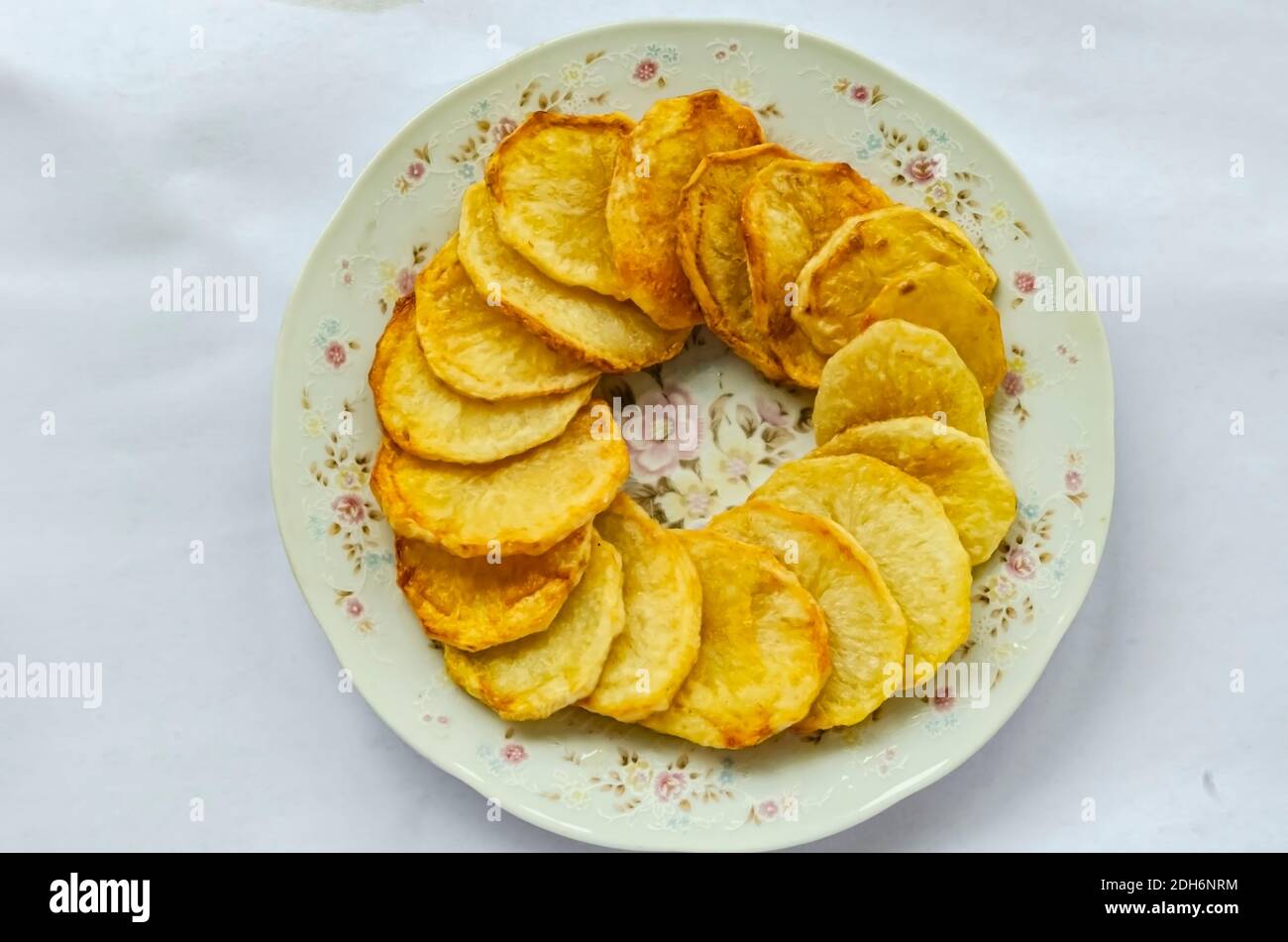On white background is a white floral plate with round slices of fried ...