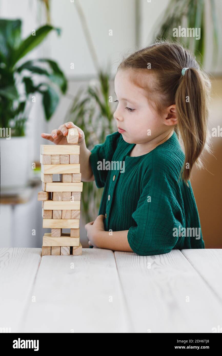 Cute little girl in green dress putting a wooden block on top of jenga ...