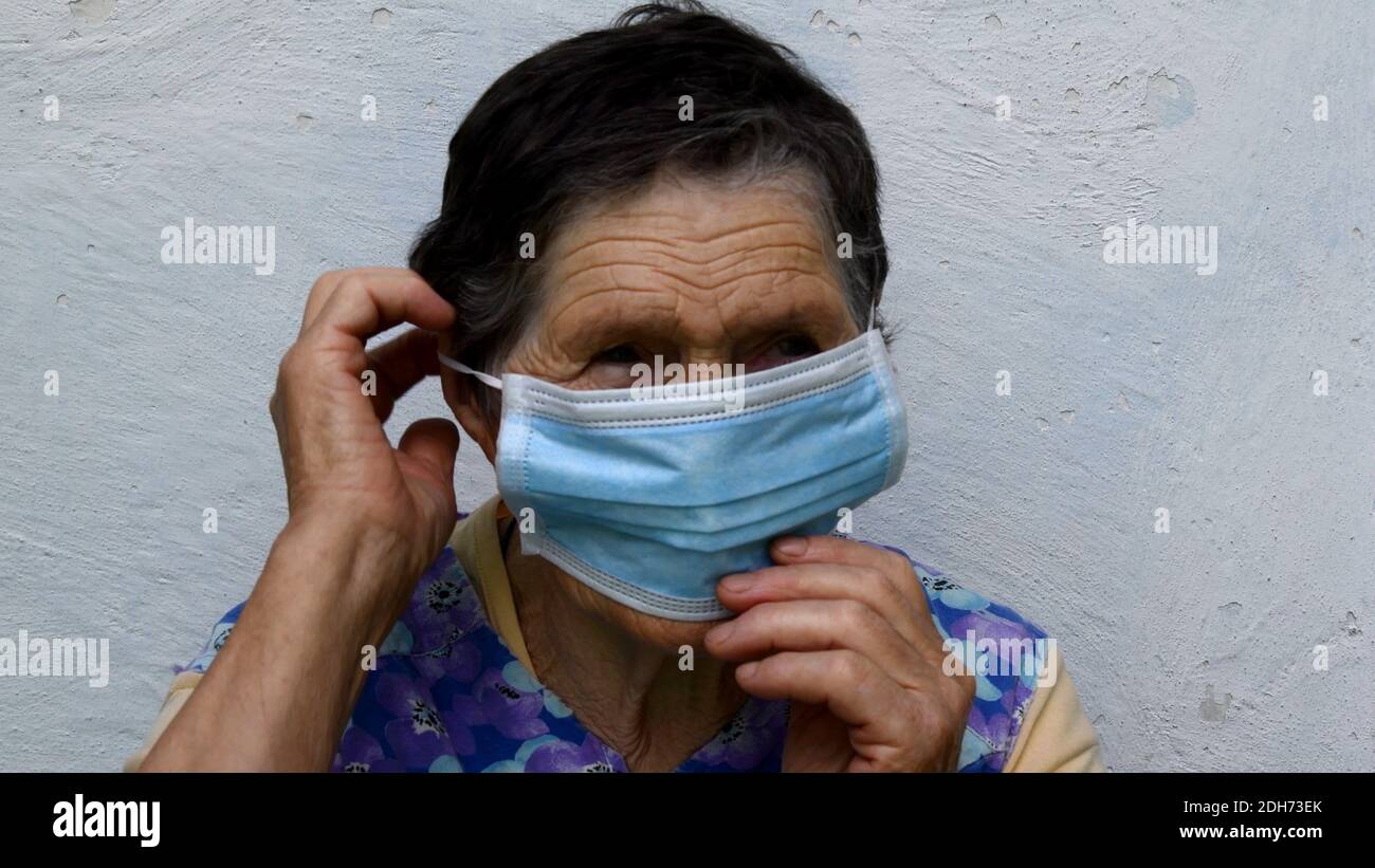 Senior woman puts on and fixes protective mask on her ear and chin ...