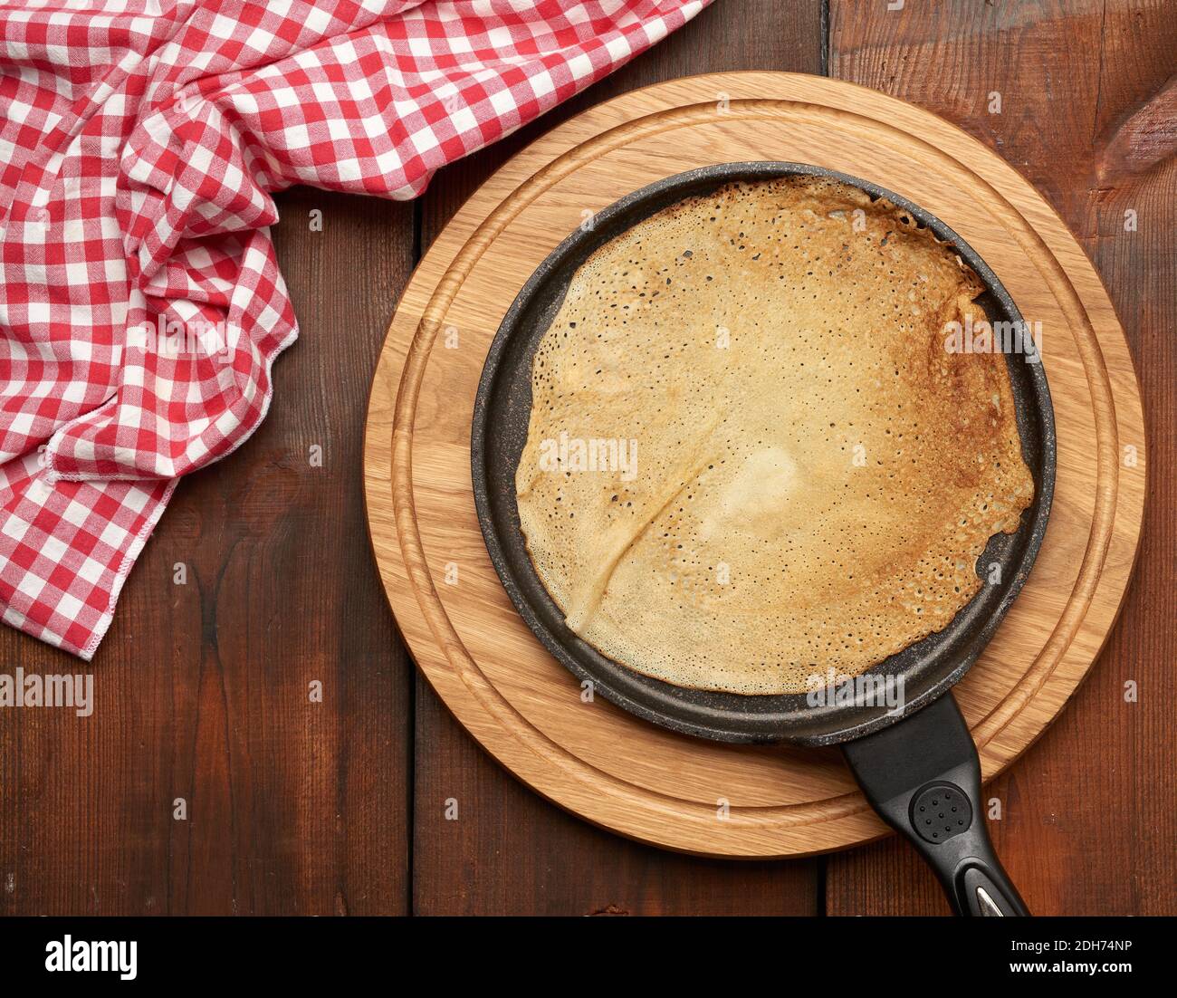 Baked round big pancake in a black frying pan on a brown wooden table ...