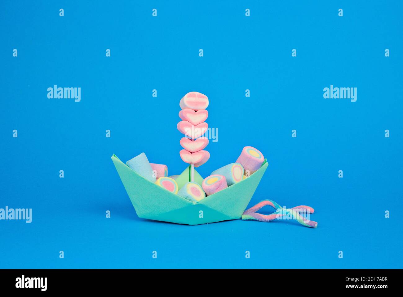 A shot of an origami paper ship full of tasty marshmallows on a pastel ...