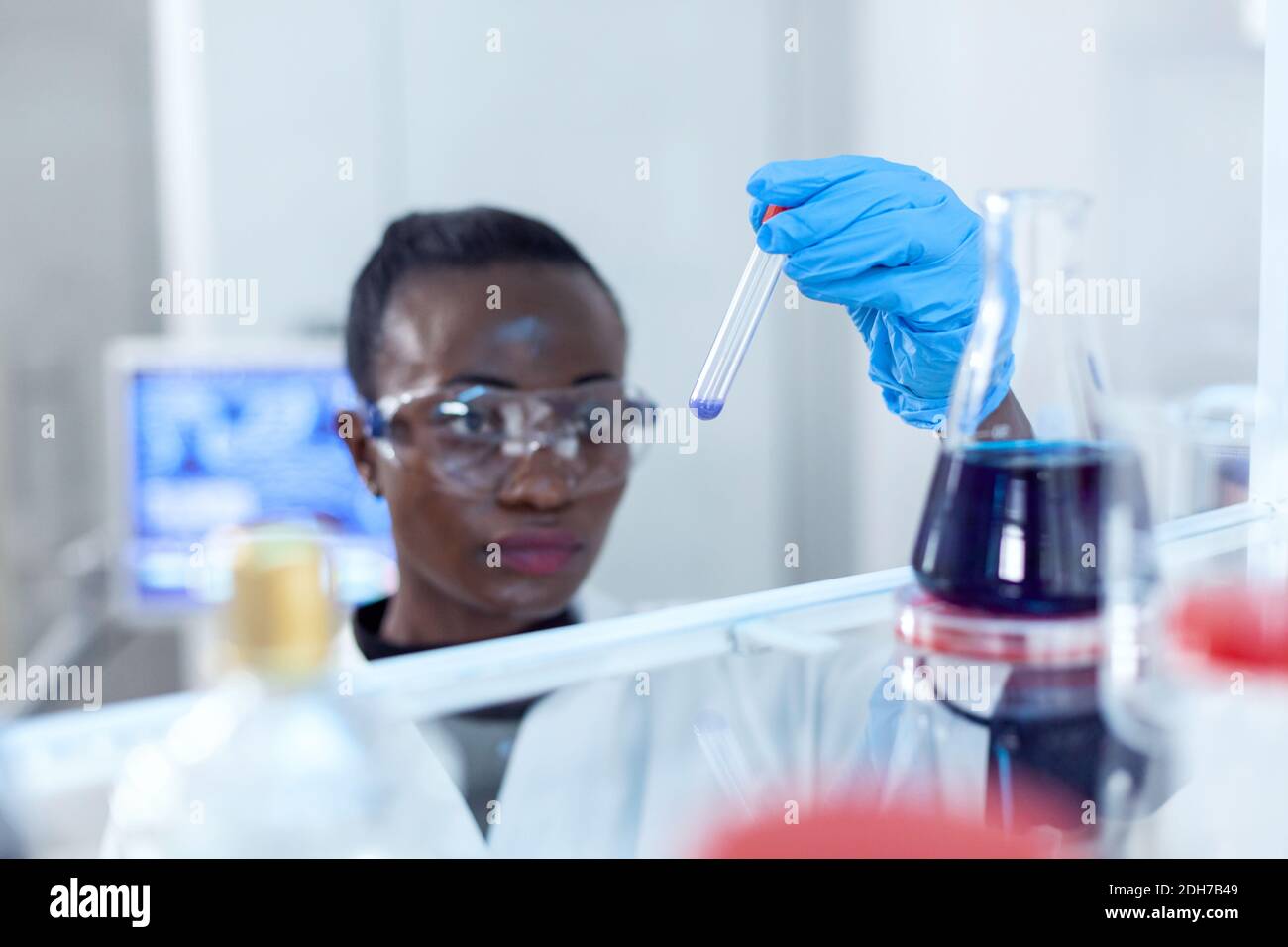 African scientist looking pensive at test tube with blue liquid. Black ...