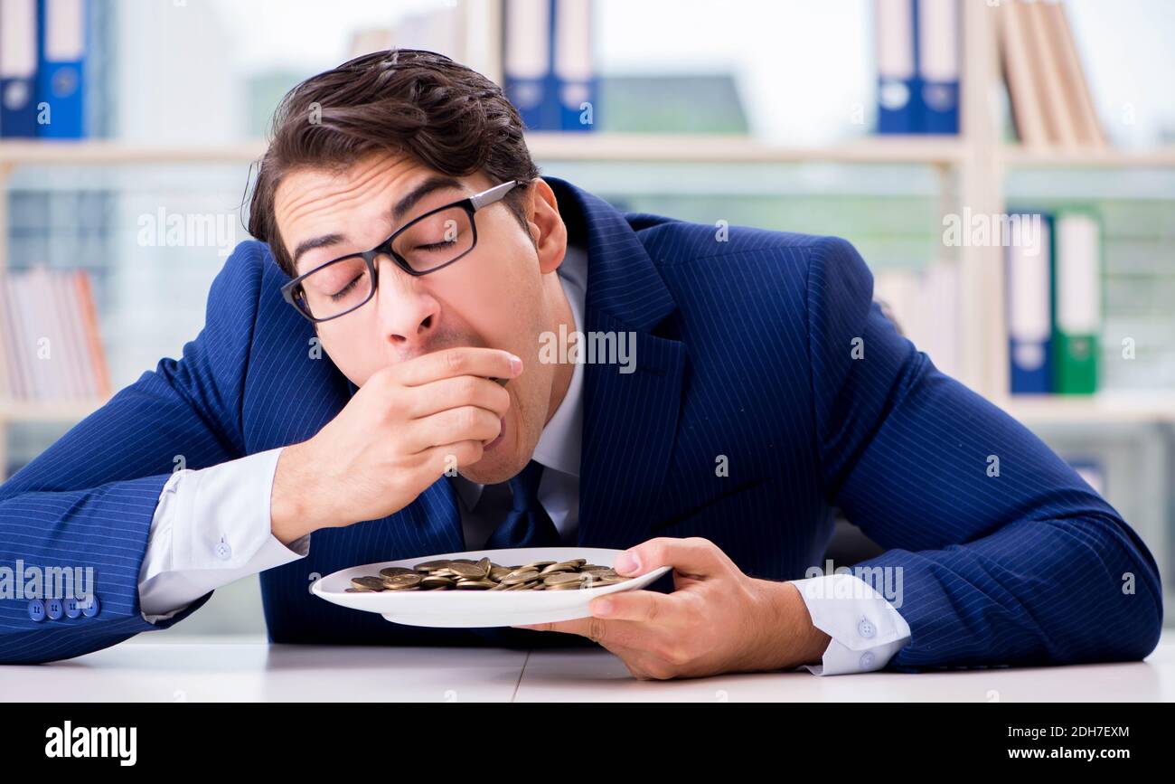 Funny businessman eating gold coins in office Stock Photo - Alamy