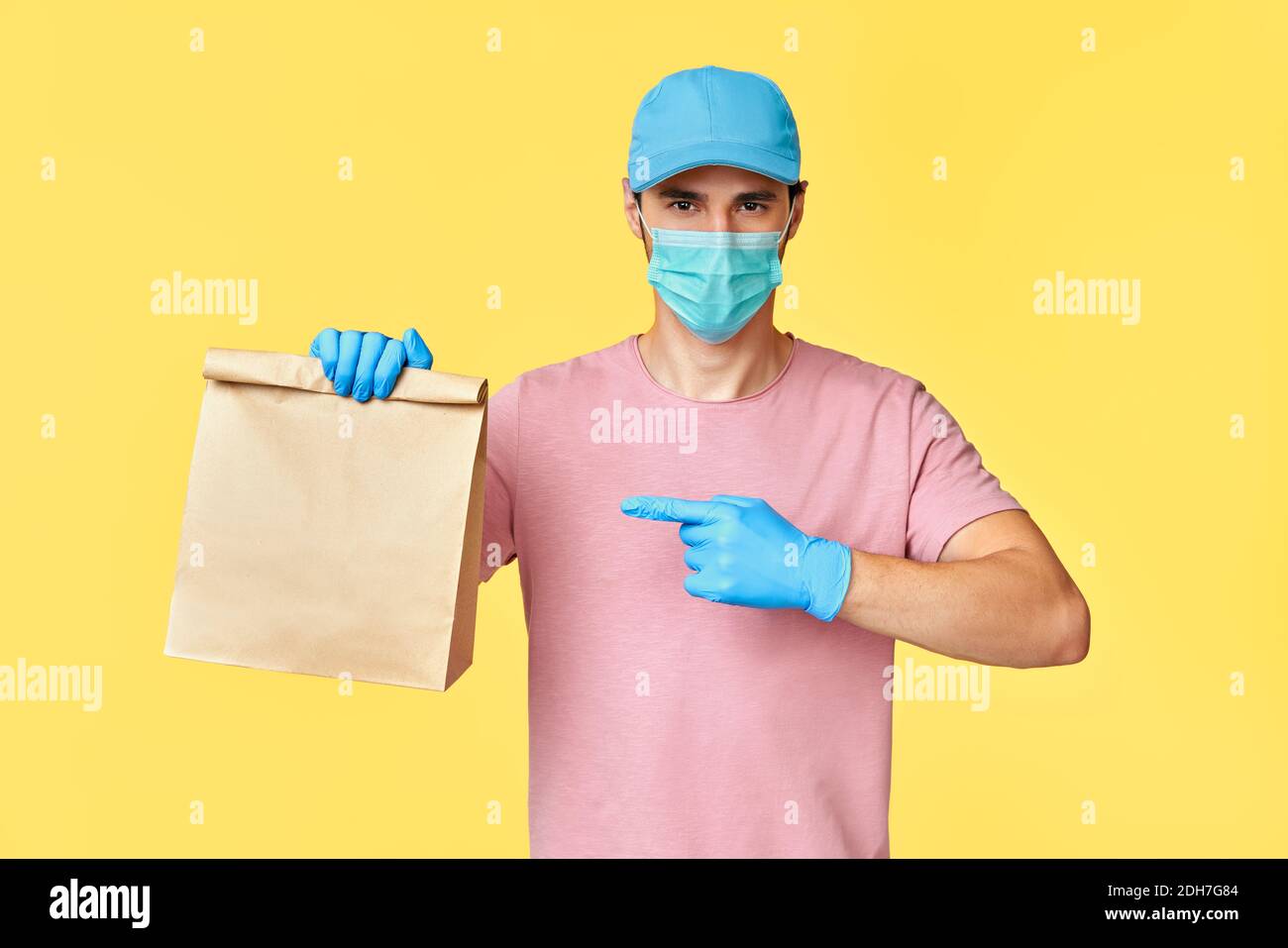Delivery man pointing on paper packet with food wearing face mask and ...