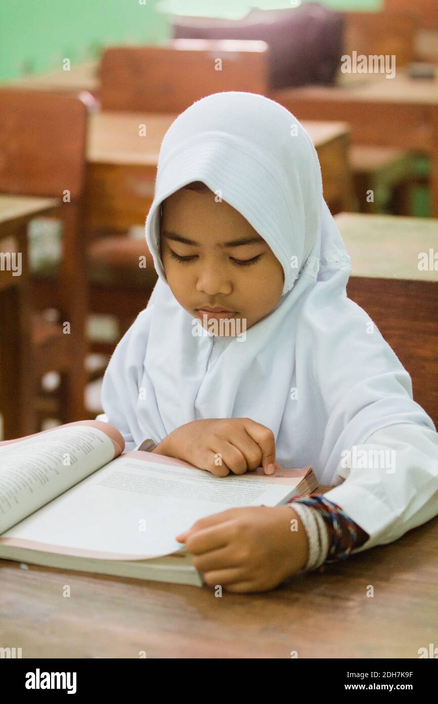 a portrait of an indonesian primary school student reading a textbook ...