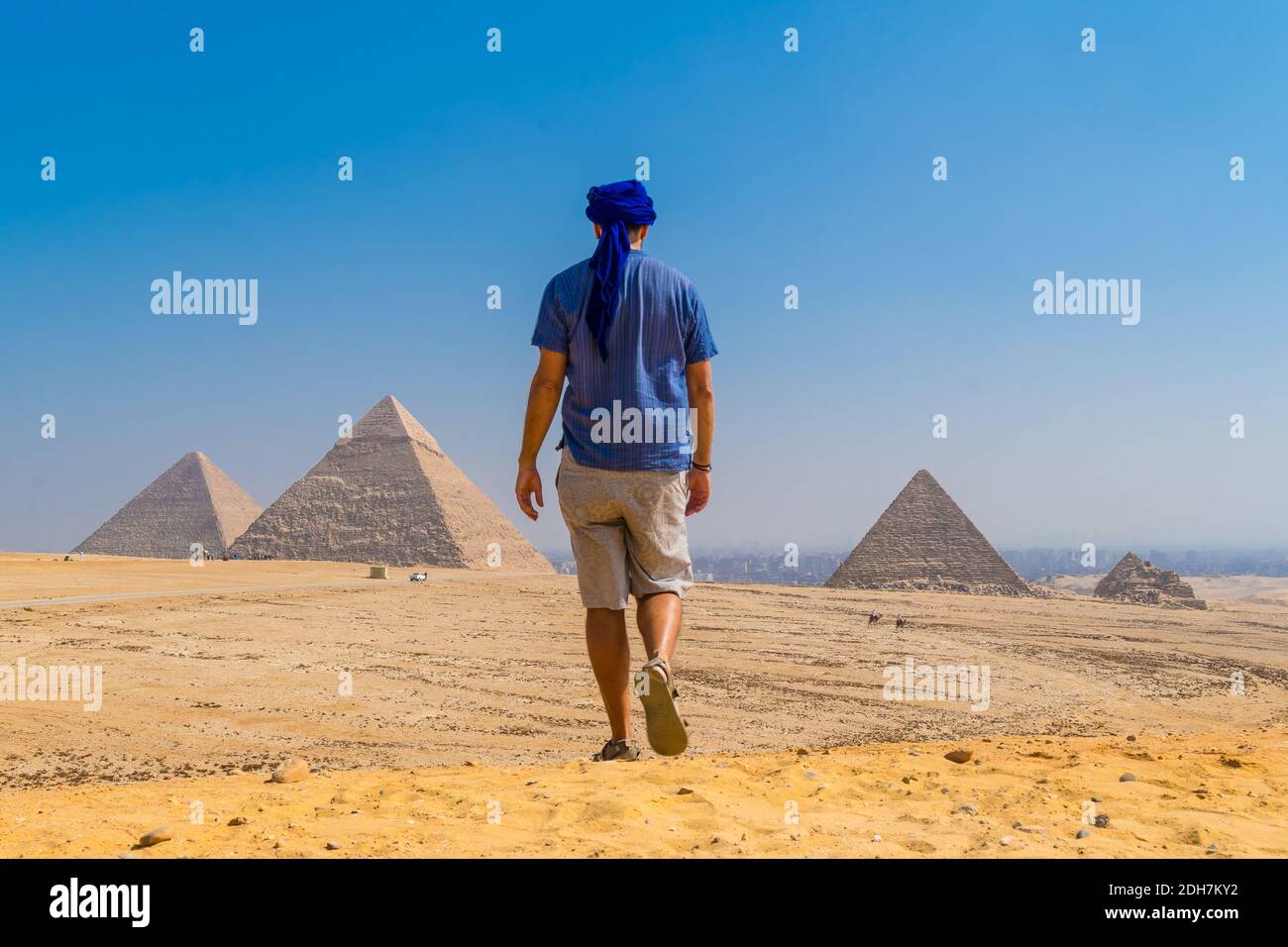 A portrait of a young man in a blue turban walking next to the Pyramids ...