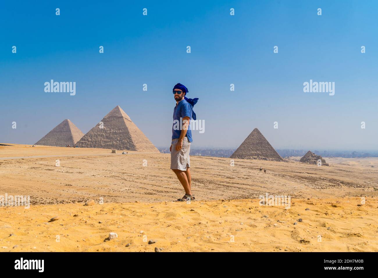 A portrait of a young man in a blue turban walking next to the Pyramids ...
