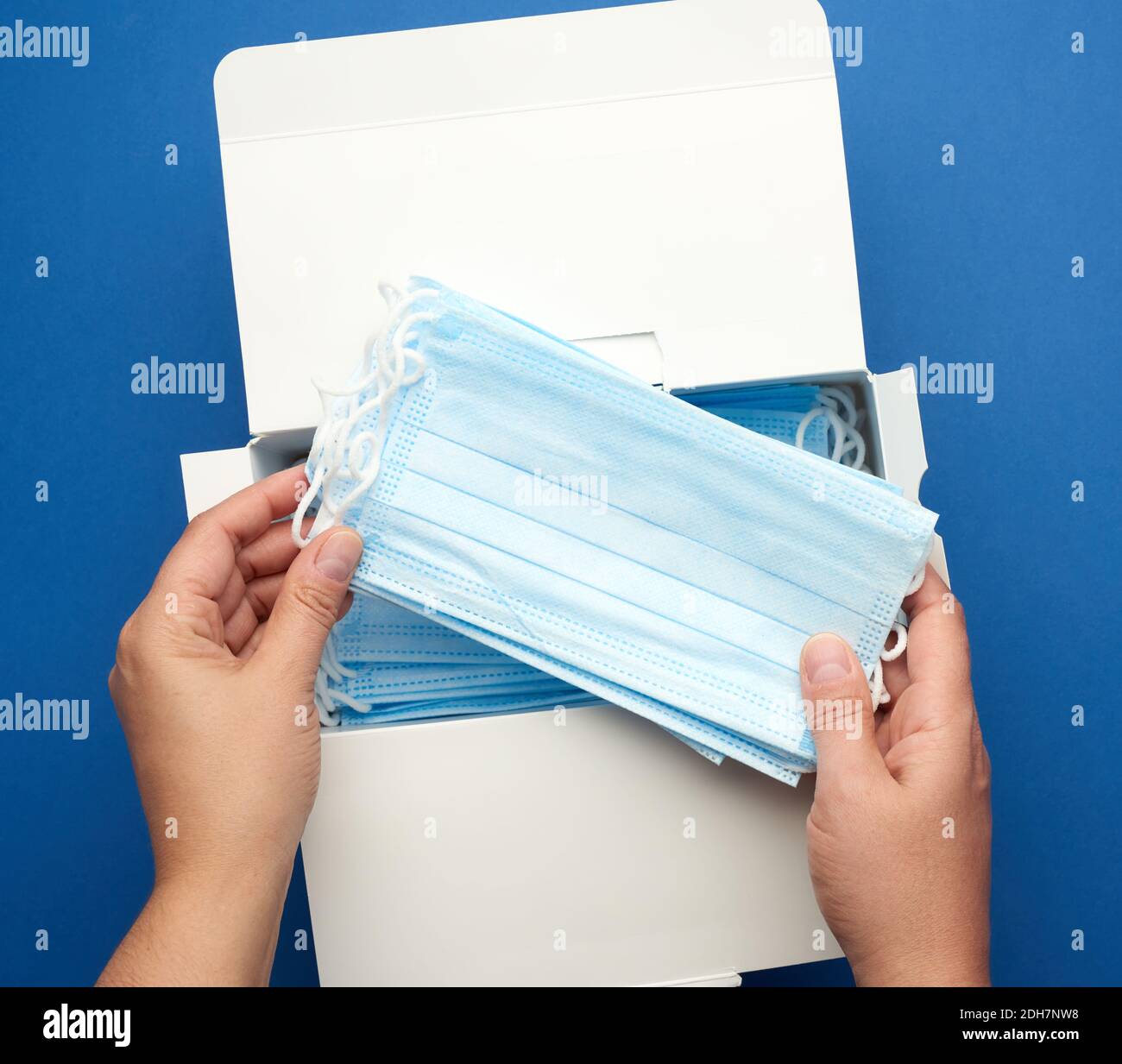 Box with disposable medical masks and two female hands, blue background ...