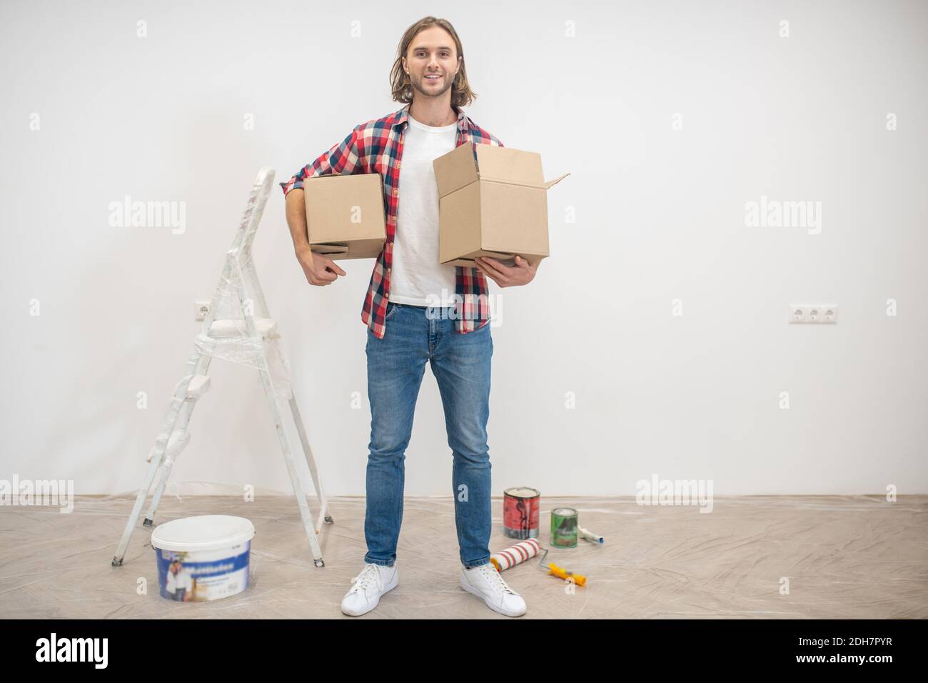 Long-haired man standing near the wall with boxes in hands Stock Photo ...