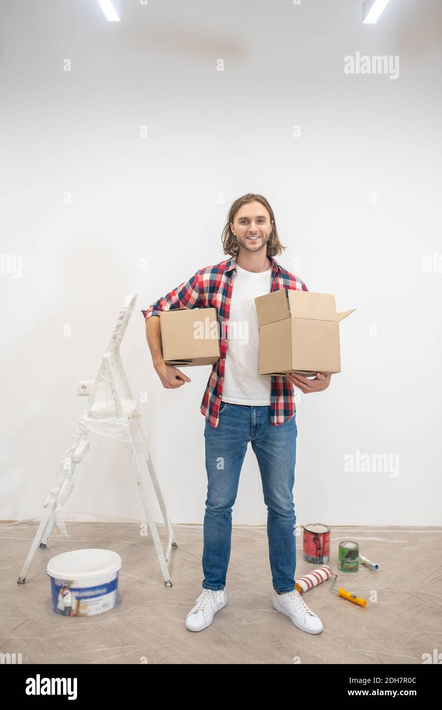 Long-haired man standing near the wall with boxes in hands Stock Photo ...