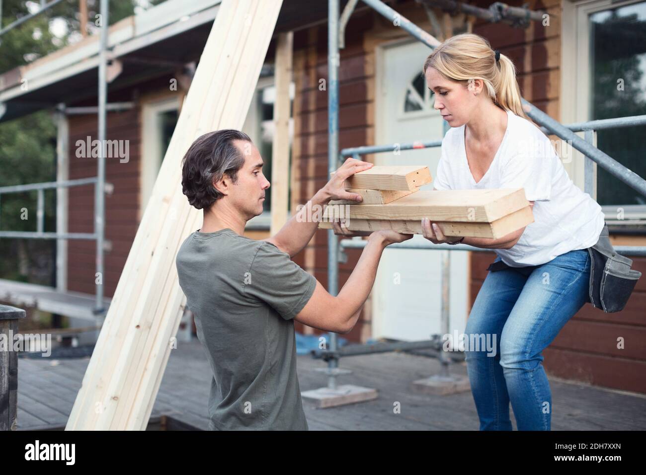 Side view of couple carrying stack of lumber outside house being ...