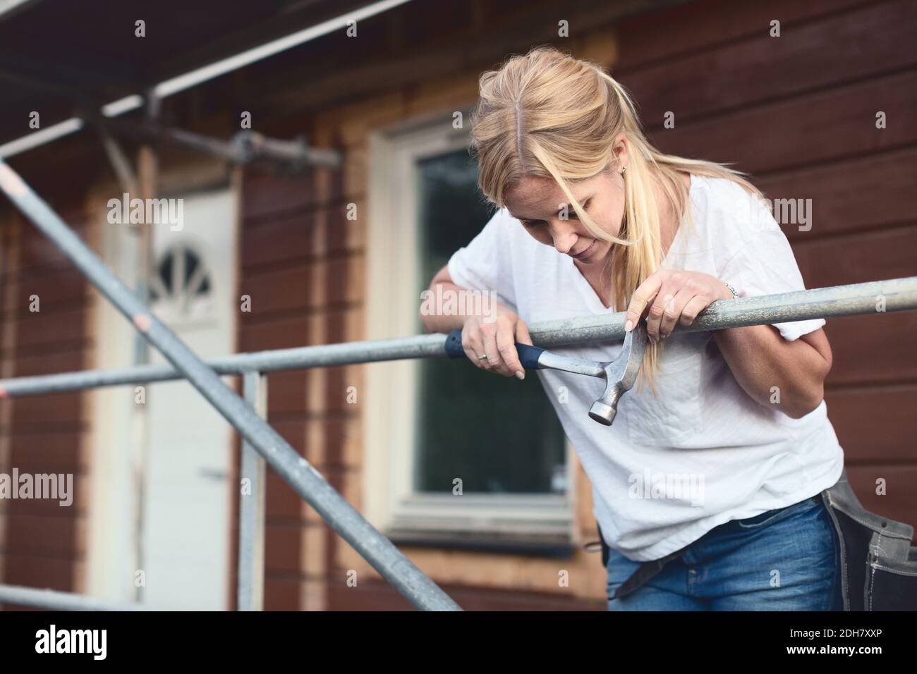 Woman holding hammer while leaning on scaffolding outside house being ...