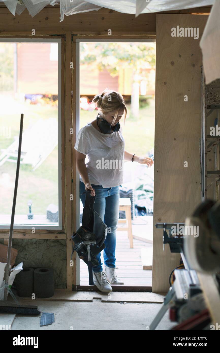 Full length of woman with tool belt entering in house being renovated ...