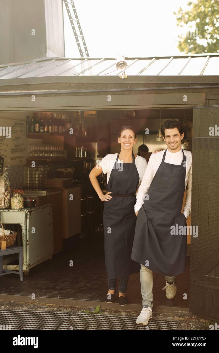 Full length portrait of smiling owners standing outside restaurant ...
