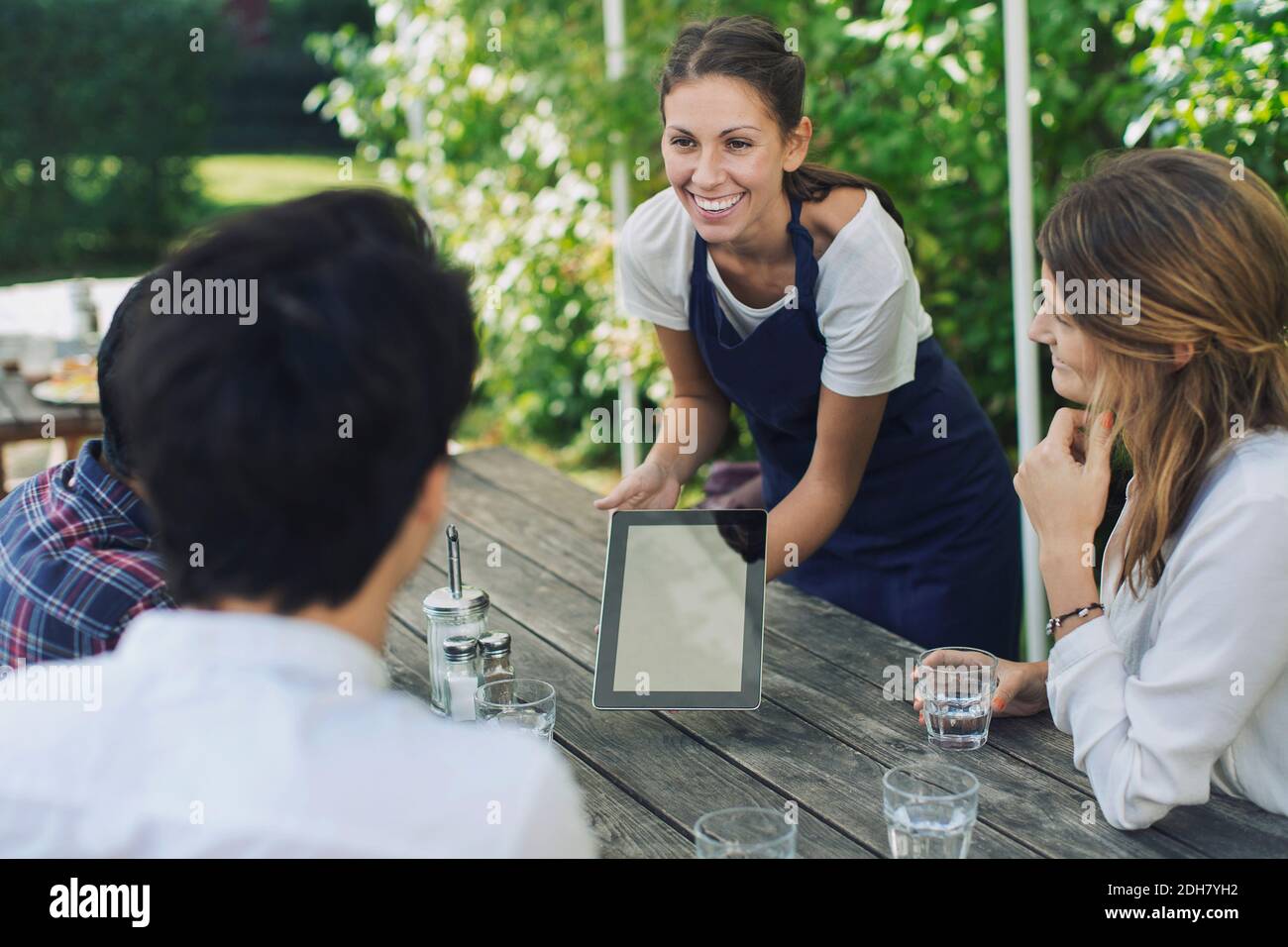 Happy waitress showing menu through digital tablet to people at outdoor ...