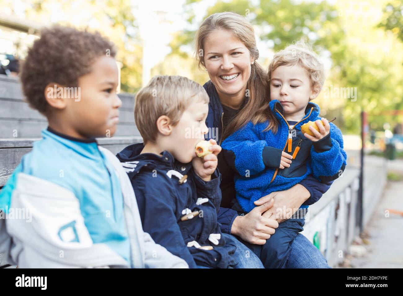 Happy teacher sitting with children outside kindergarten Stock Photo ...